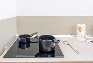Uma cozinha com um fogão por indução preto, duas panelas pretas, uma espátula e um rolo de papel toalha.