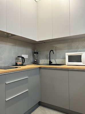 Uma cozinha moderna com armários cinza, bancada de madeira, cafeteira, liquidificador e micro-ondas.
