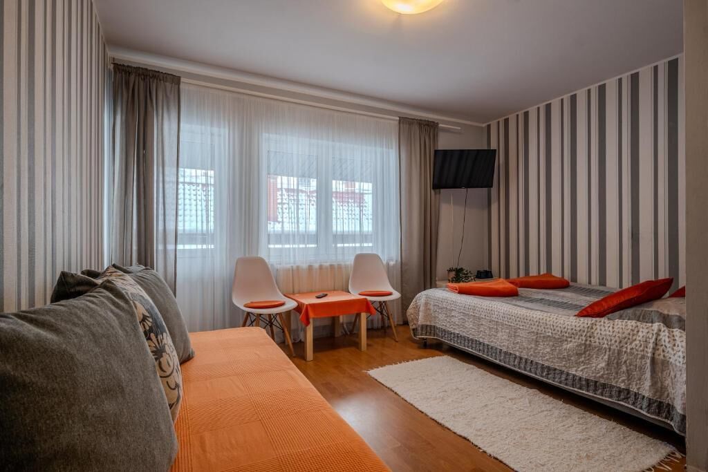 Quarto de hotel com cama, sofá, mesa e cadeiras, e uma televisão.