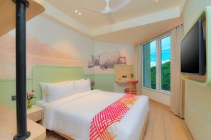 Quarto de hotel com cama, escrivaninha, cadeira, televisão e uma janela grande.
