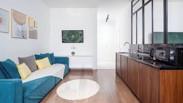 Uma sala de estar moderna com um sofá azul, um tapete branco e uma área de cozinha com micro-ondas e pia.