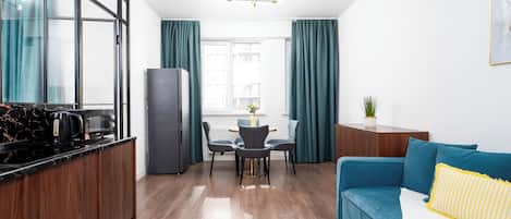 Uma sala moderna com um sofá azul, uma área de cozinha com geladeira e uma mesa de jantar com cadeiras.