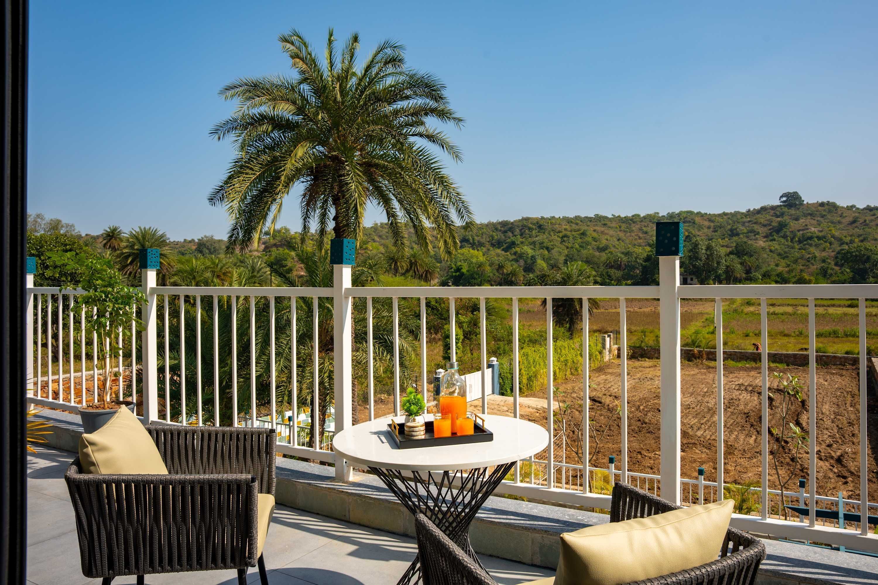 Uma varanda com móveis de vime, uma mesa com uma bandeja de suco de laranja e vista para uma palmeira e paisagem montanhosa.