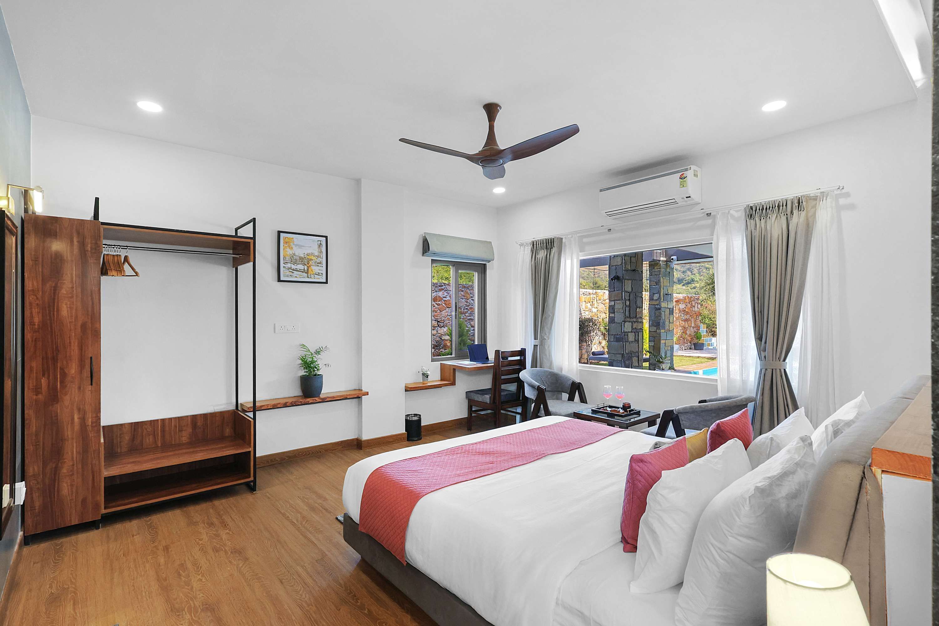 Quarto com cama, escrivaninha, cadeira, guarda-roupa, ventoinha no teto e janela com cortinas.