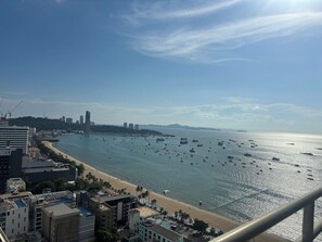 Paisagem costeira com praia, barcos e edifícios altos.