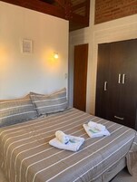 Quarto de hotel com cama, almofadas, guarda-roupa e luminária fixada na parede.