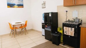 Cozinha compacta com mesa, cadeiras, geladeira, fogão e lixeira.