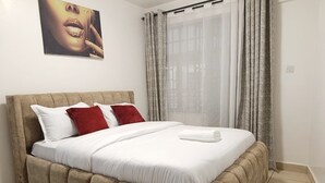 Uma cama com cabeceira, roupa de cama branca e um travesseiro vermelho.
