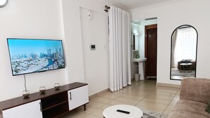 Sala de estar com televisão de tela plana, sofá, mesa de centro e vista para um banheiro.