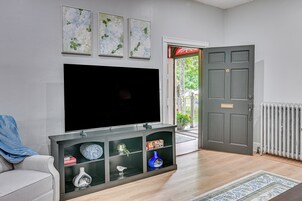 Sala de estar com televisão de tela plana, sofá, mesa de centro com objetos decorativos e uma porta que dá para o exterior.