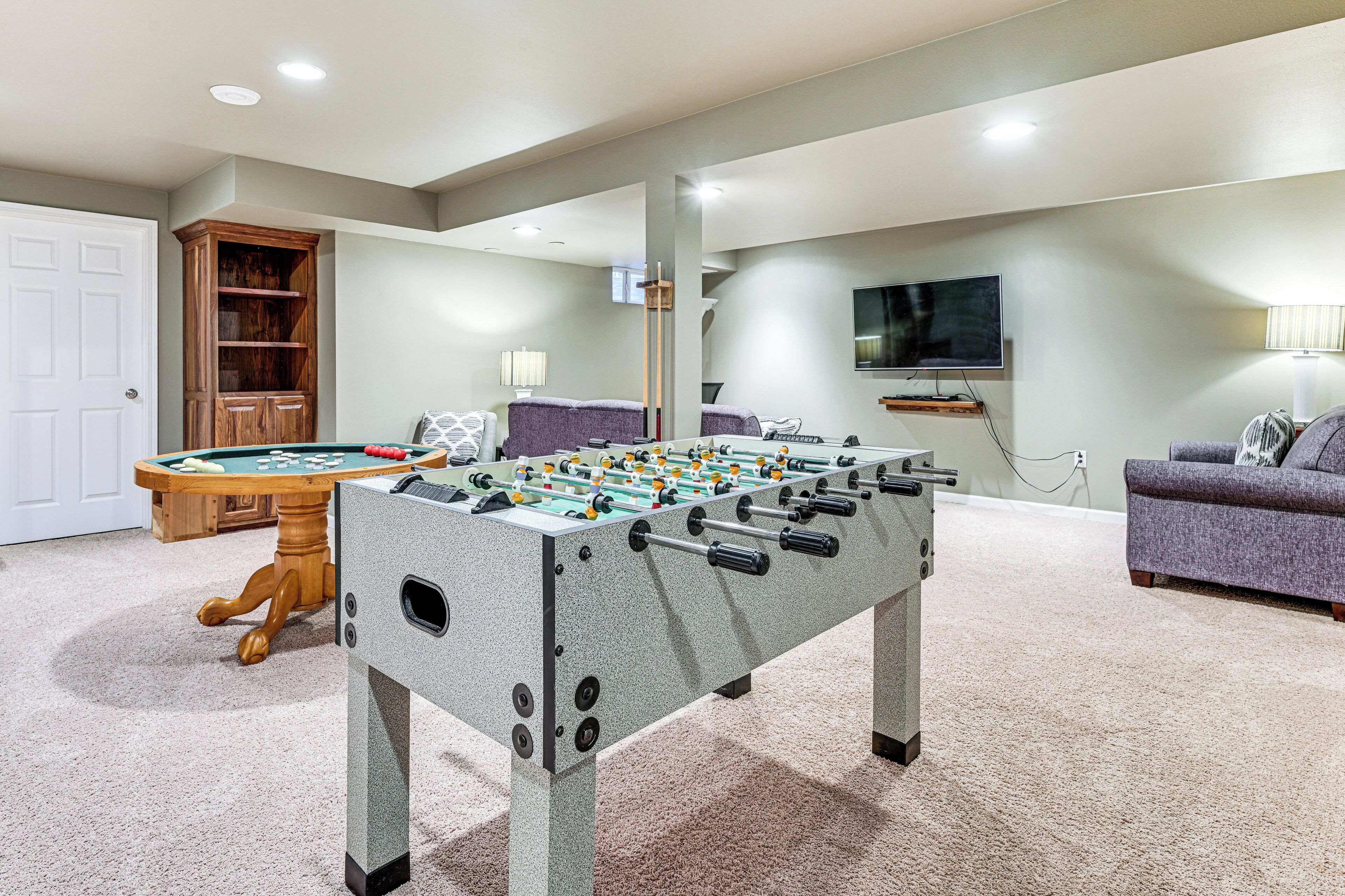 Um quarto com mesa de futebol, mesa de bilhar, sofá e televisão na parede.