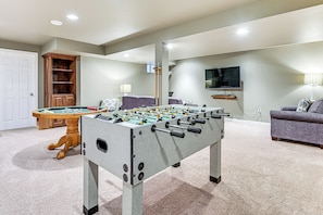 Um quarto com mesa de futebol, mesa de bilhar, sofá e televisão na parede.