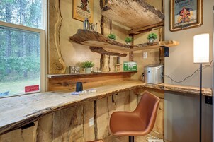 Interior de cabana com paredes de madeira rústica, área de bar com uma garrafa e dados, uma cadeira e uma placa que indica que a cabana é um lugar feliz.