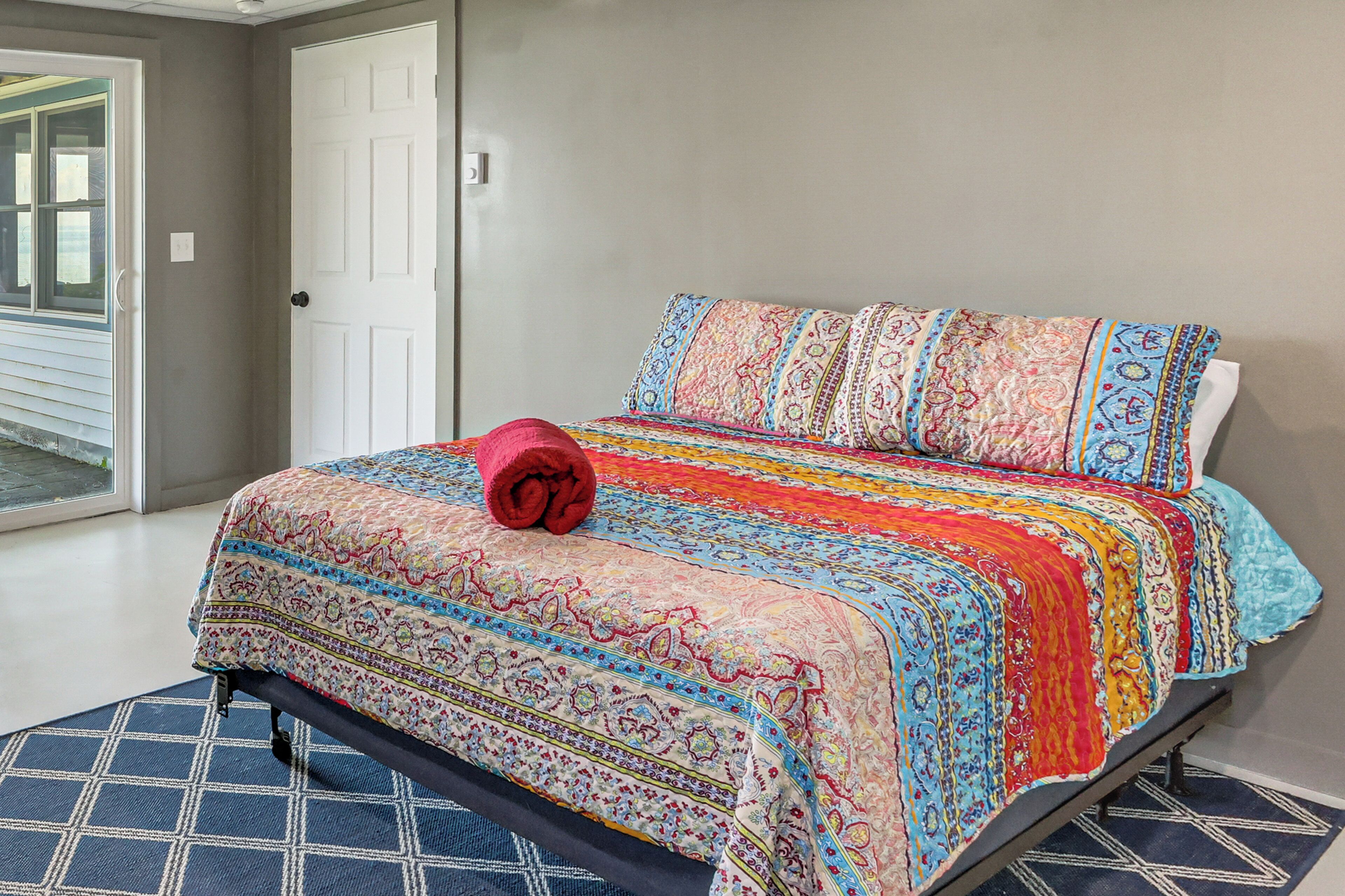 Quarto com cama, colcha estampada, manta enrolada e tapete azul.