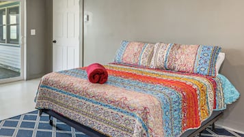 Quarto com cama, colcha estampada, manta enrolada e tapete azul.