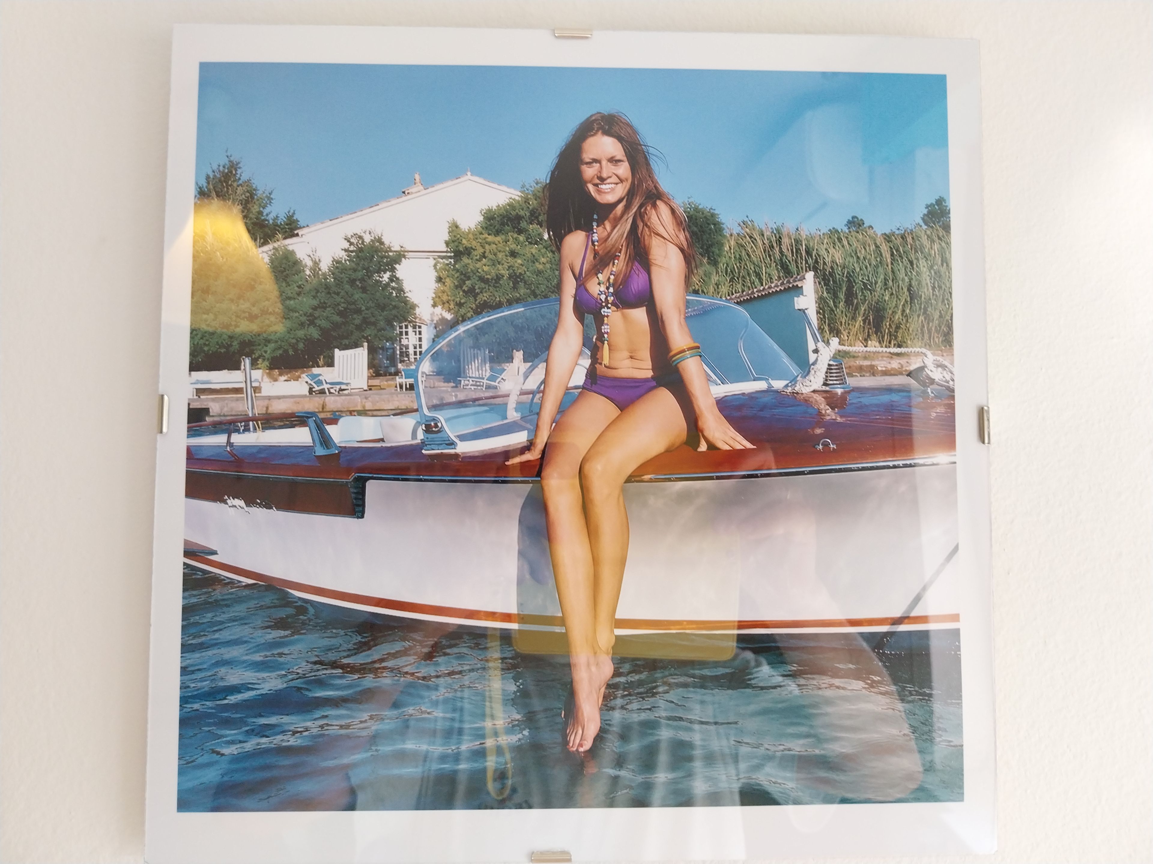 Uma mulher sentada na borda de um barco, com vista para a água e um prédio ao fundo.
