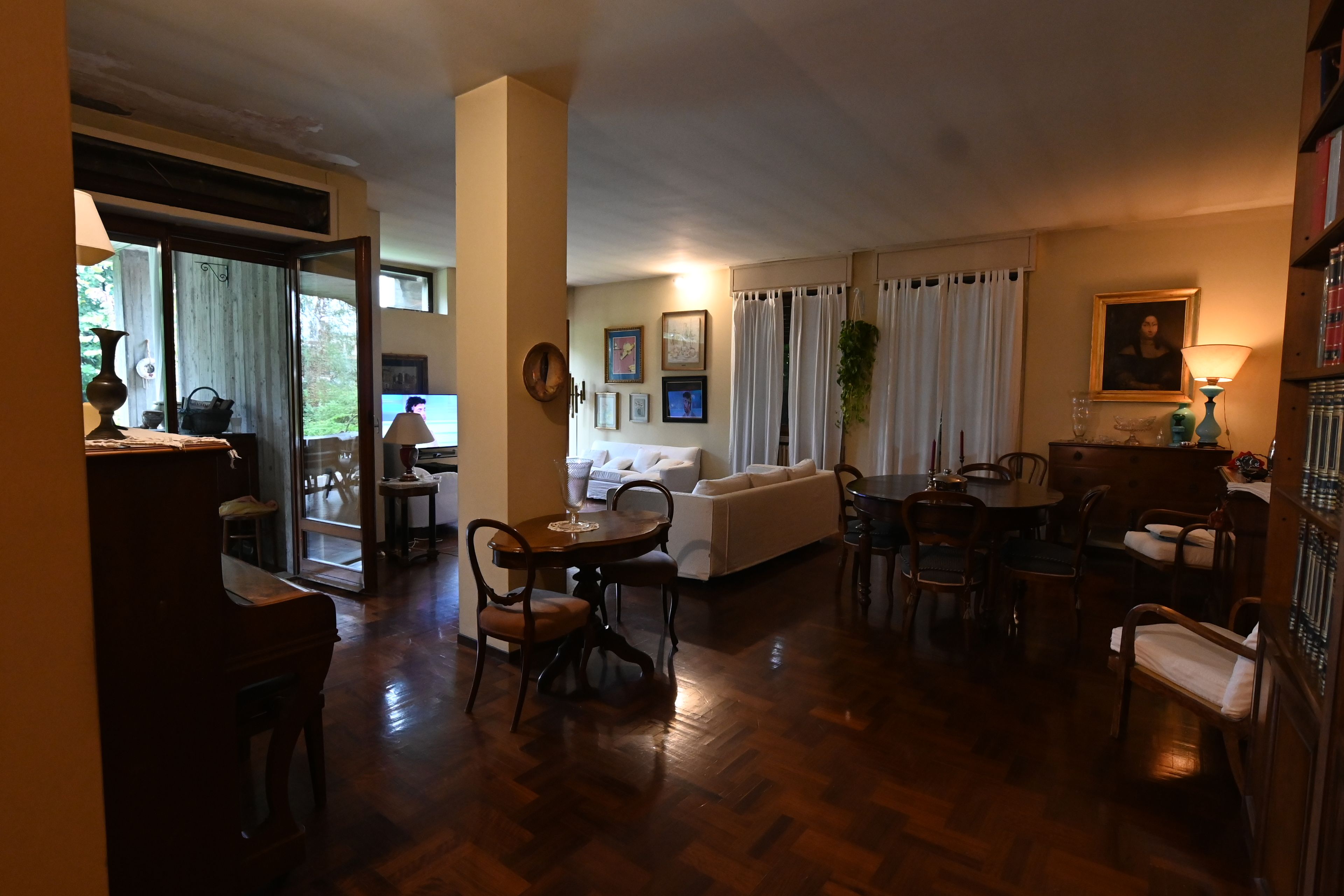 Uma sala de estar espaçosa com piso de madeira, um sofá branco, uma mesa de jantar com cadeiras e uma cozinha com fogão e armários.