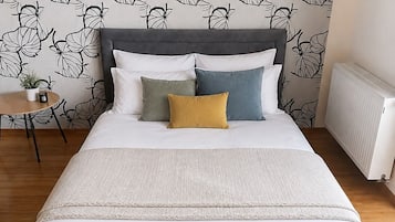 Quarto com uma cama, almofadas, mesa de cabeceira e parede com padrão de folha.