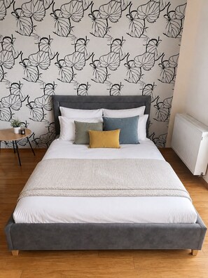Quarto com uma cama, almofadas, mesa de cabeceira e parede com padrão de folha.