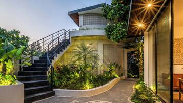 Um edifício moderno com uma escadaria que leva a uma varanda, rodeado por vegetação exuberante.