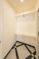 Um banheiro pequeno e fechado, com piso de azulejo, porta branca e um armário com prateleiras.