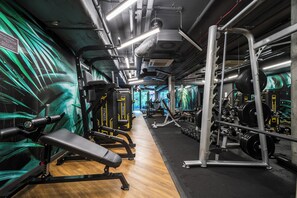 Uma academia com diversos equipamentos de ginástica, um banco e uma parede com um design abstrato em verde.