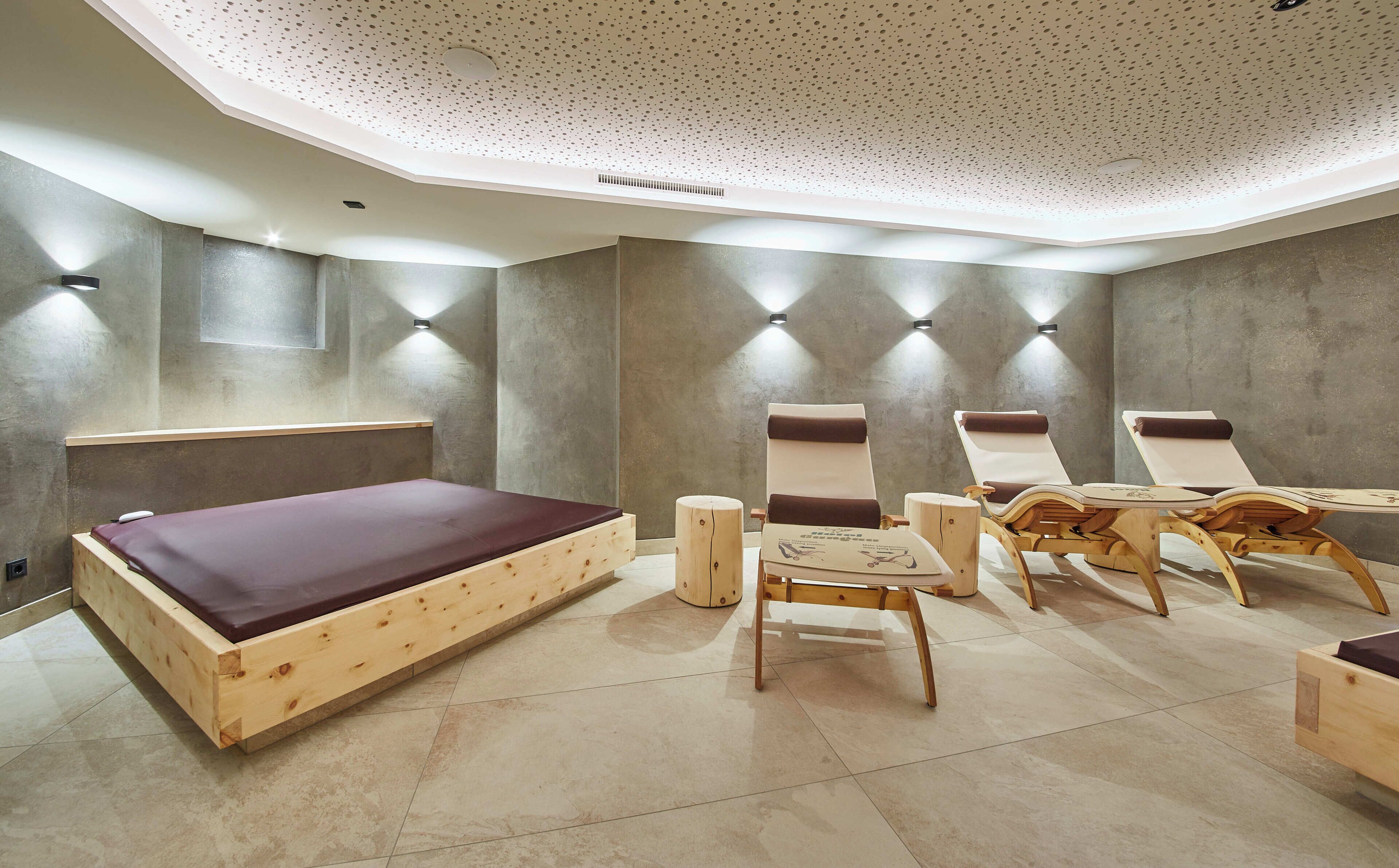 Quarto moderno com cama de madeira, duas poltronas, uma mesinha de madeira e teto com design perfurado.