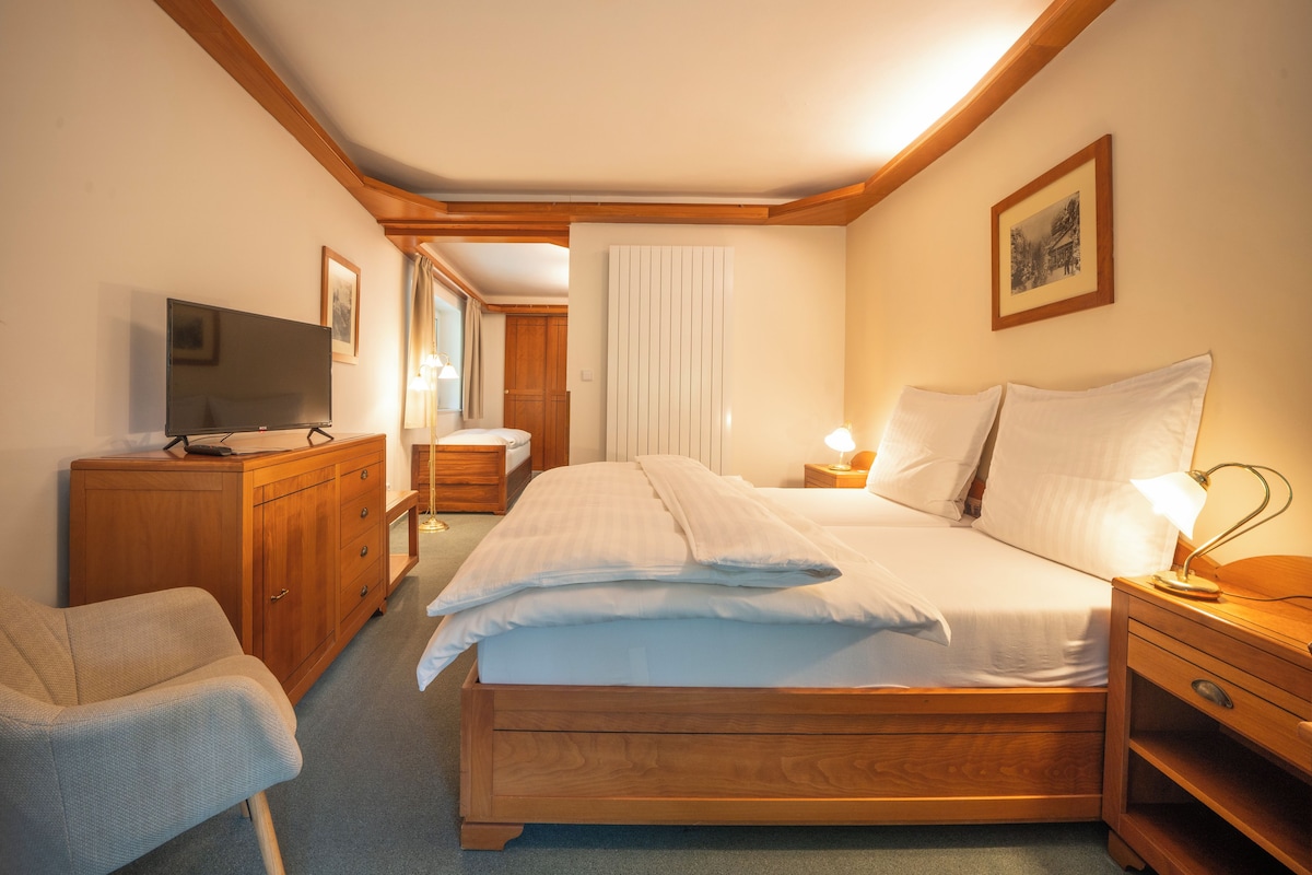 Um quarto com cama, mesas de cabeceira, televisão, poltrona e guarda-roupa.