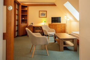 Quarto compacto com uma mesa de jantar, duas cadeiras, televisão, escrivaninha com luminária, estante de livros e uma cama.