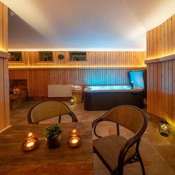 Quarto aconchegante com painel de madeira, banheira de hidromassagem e mesa de jantar com velas.