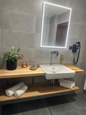 Uma casa de banho moderna com uma pia branca, um espelho com iluminação LED, uma planta em vaso e um porta-toalhas.