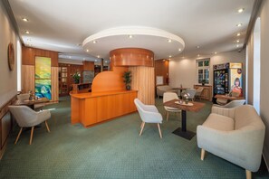 Um saguão de hotel com balcão de recepção, área de estar e um café.