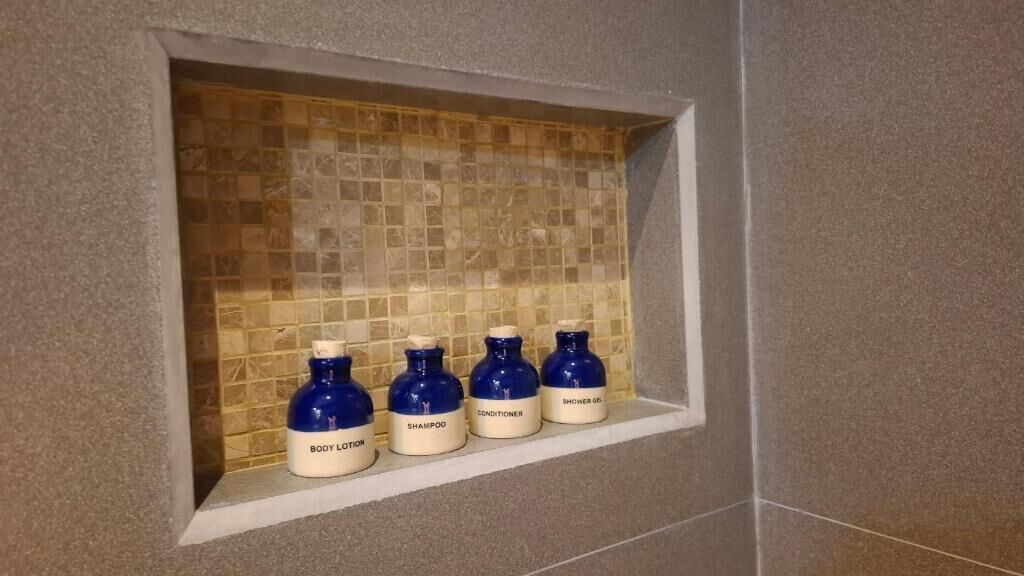 Uma prateleira no banheiro com cinco frascos de loção corporal, shampoo, condicionador e gel de banho.