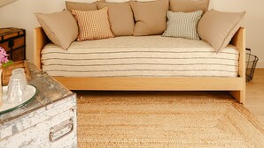Uma sala de estar aconchegante com um sofá, um tapete tecido, um baú de madeira e uma escada.