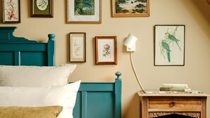 Quarto com cama, mesa de cabeceira e parede decorada com gravuras botânicas emolduradas.