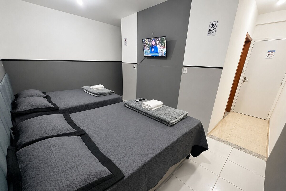 Quarto de hotel com duas camas, televisão fixada na parede e uma porta com um aviso.