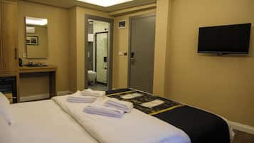 Quarto de hotel com cama, televisão, banheiro e escrivaninha com telefone.