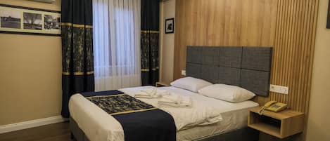 Quarto de hotel com cama, telefone de apoio e mesa de cabeceira.