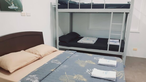 Uma cama beliche com uma cama inferior e um beliche superior. Há uma cama à esquerda, com cabeceira e almofadas.