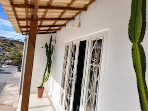 Um edifício com fachada branca, pérgola de madeira e um cacto em vaso.