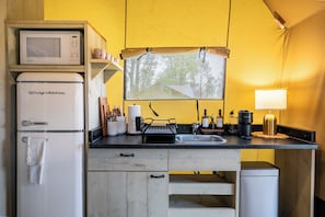 A compact kitchenette with a microwave, a refrigerator, a sink, and a window with a view of trees.