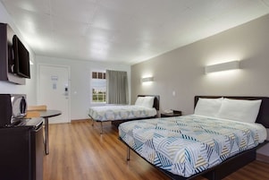 Quarto de hotel com duas camas, uma mesa, televisão e janela com cortinas.