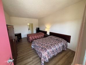 Quarto de hotel com duas camas, uma escrivaninha, uma cadeira, um guarda-roupa e um espelho.