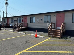 Um motel com porta vermelha, escadaria e estacionamento com linhas amarelas.