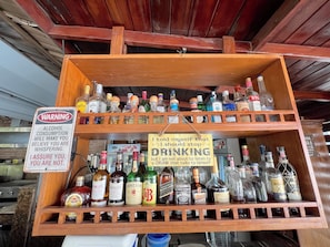 Uma prateleira de madeira com várias garrafas de bebidas alcoólicas e duas placas, uma alertando sobre o consumo de álcool e a outra aconselhando a não beber.