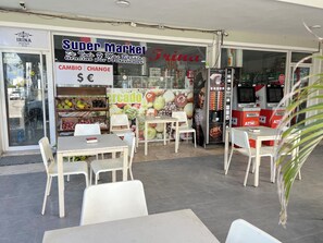 Um supermercado com uma placa 'CAMBIO CHANGE', uma placa 'Mercado' e uma máquina de vendas automática 'Cafe World'.