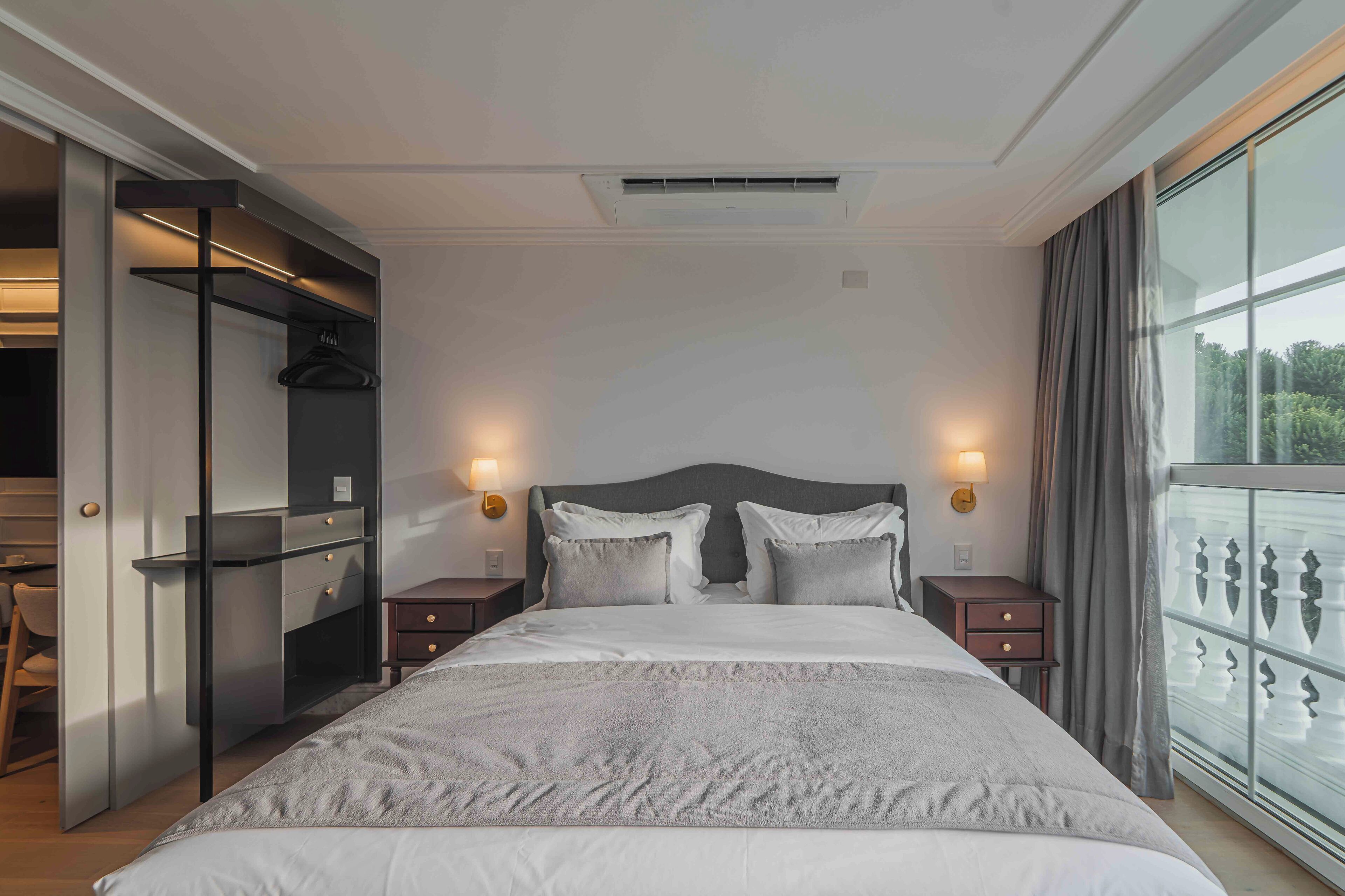 Quarto de hotel com uma cama grande, um guarda-roupa, uma mesa de cabeceira e uma janela com vista.