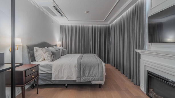 Quarto moderno com cama, mesas de cabeceira, lareira e cortinas.