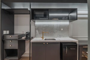 Uma cozinha compacta com micro-ondas integrado, cafeteira e geladeira.