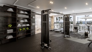 Uma academia com equipamentos de exercícios, uma parede de mármore e prateleiras com toalhas e garrafas.